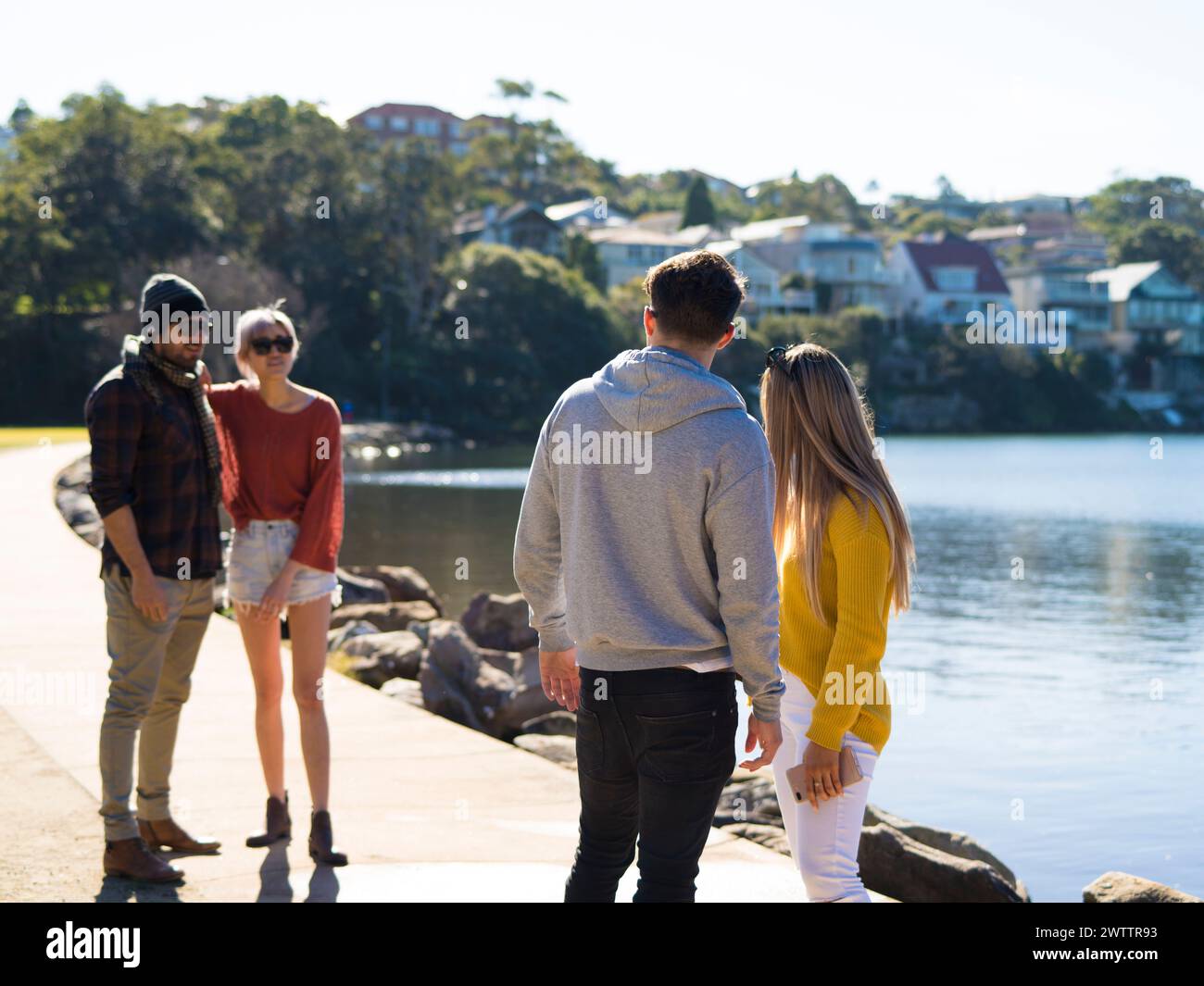 Four friends by a lakeside with houses in the background Stock Photo ...