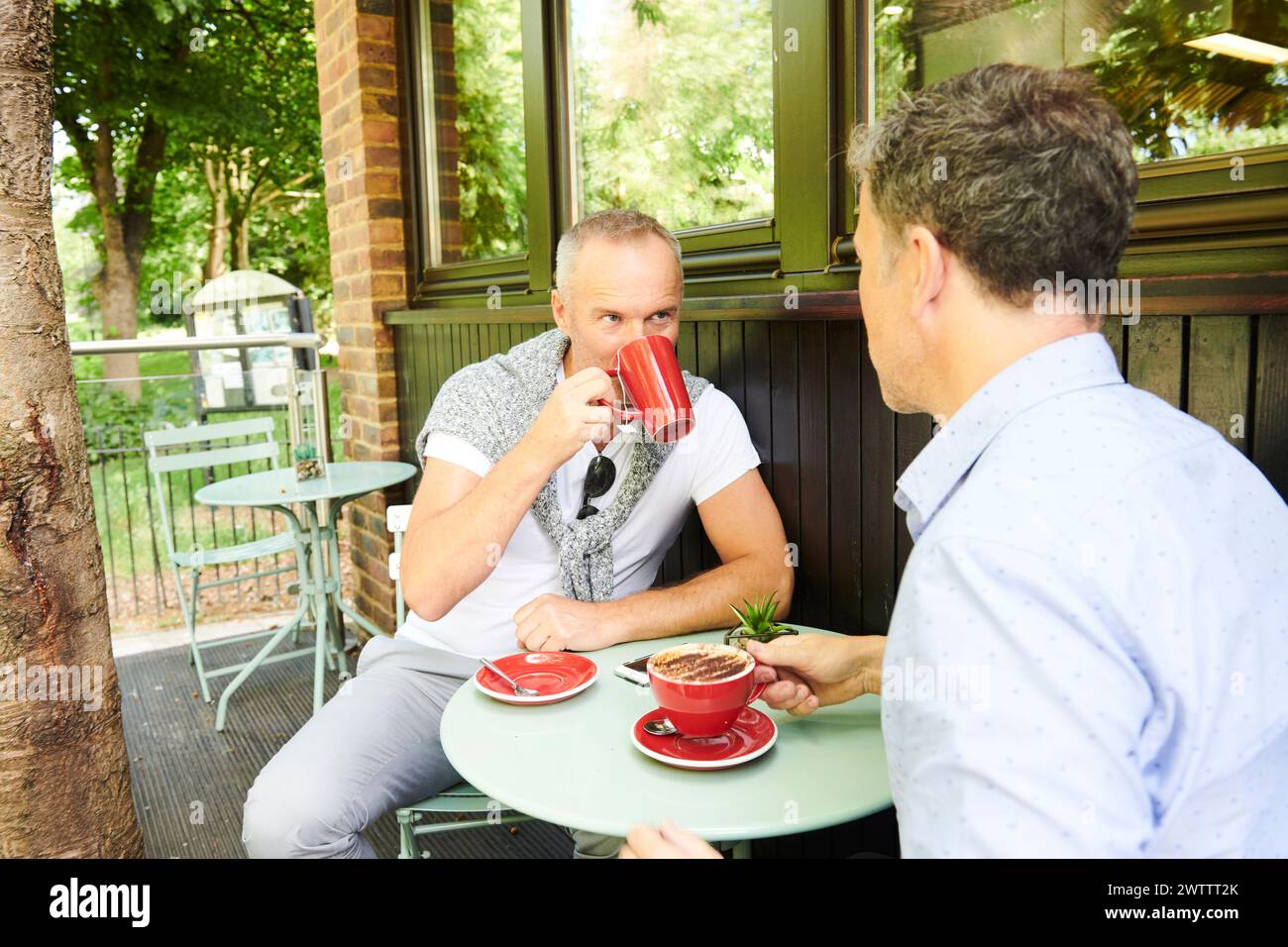 Two men enjoying a coffee conversation outdoors Stock Photo - Alamy