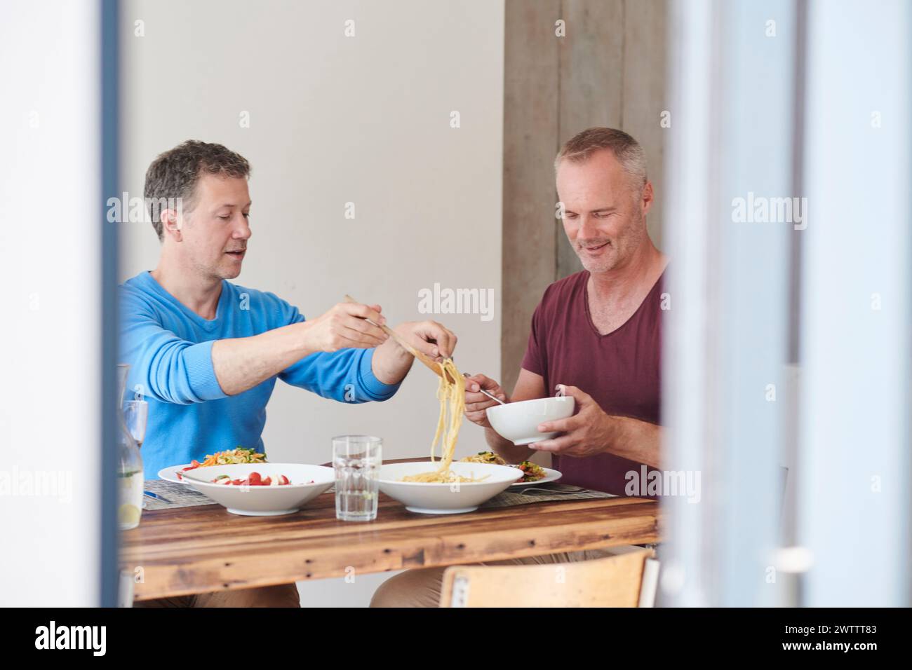 Two men enjoying pasta at a dining table Stock Photo - Alamy