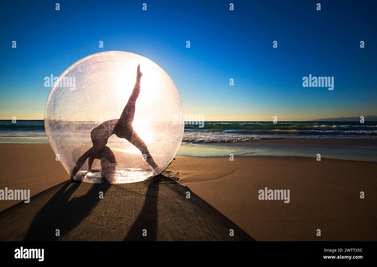 Person performing a handstand inside a transparent sphere on the beach ...