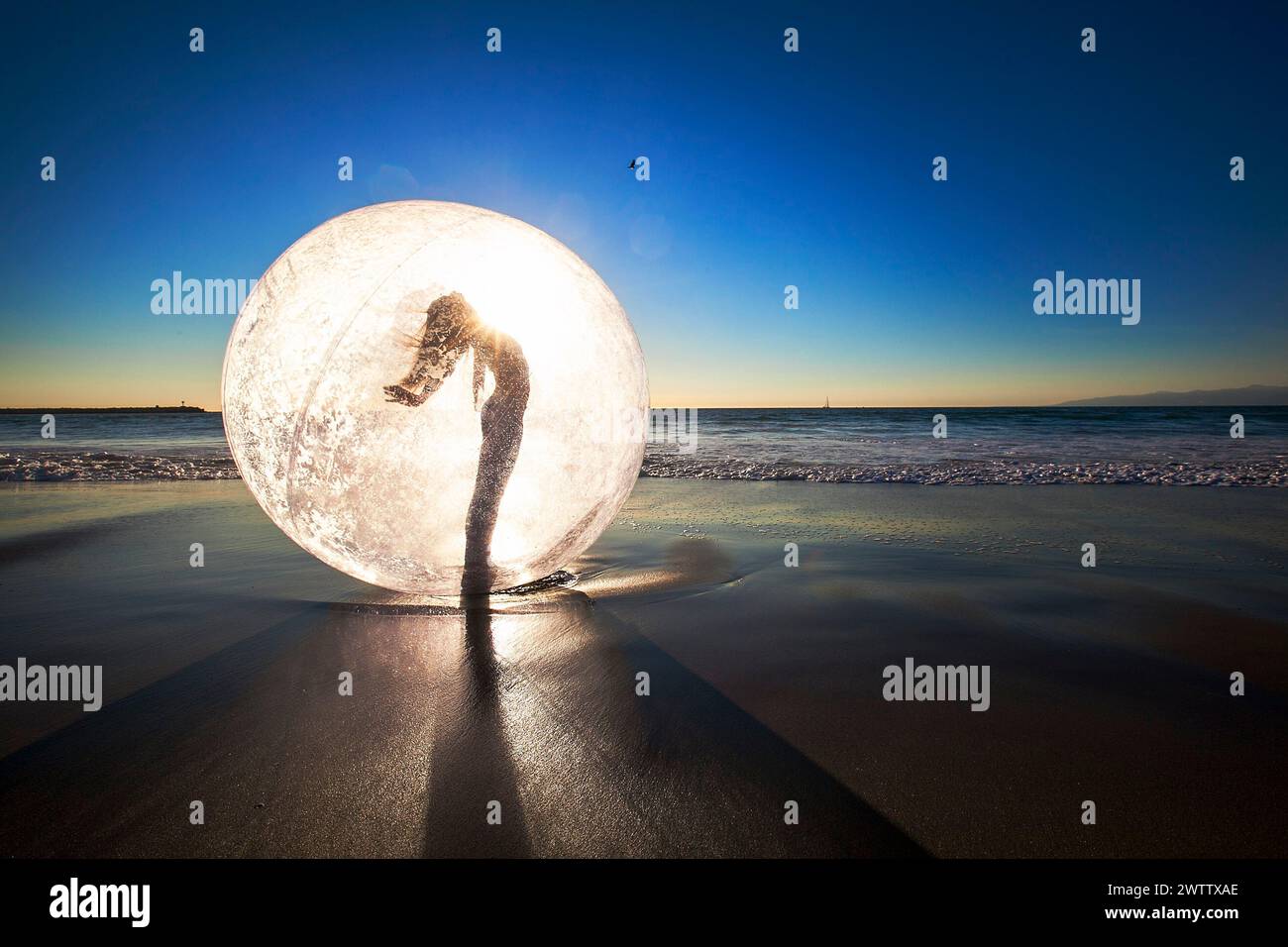 Silhouette of a person inside a translucent sphere on a beach at sunset ...