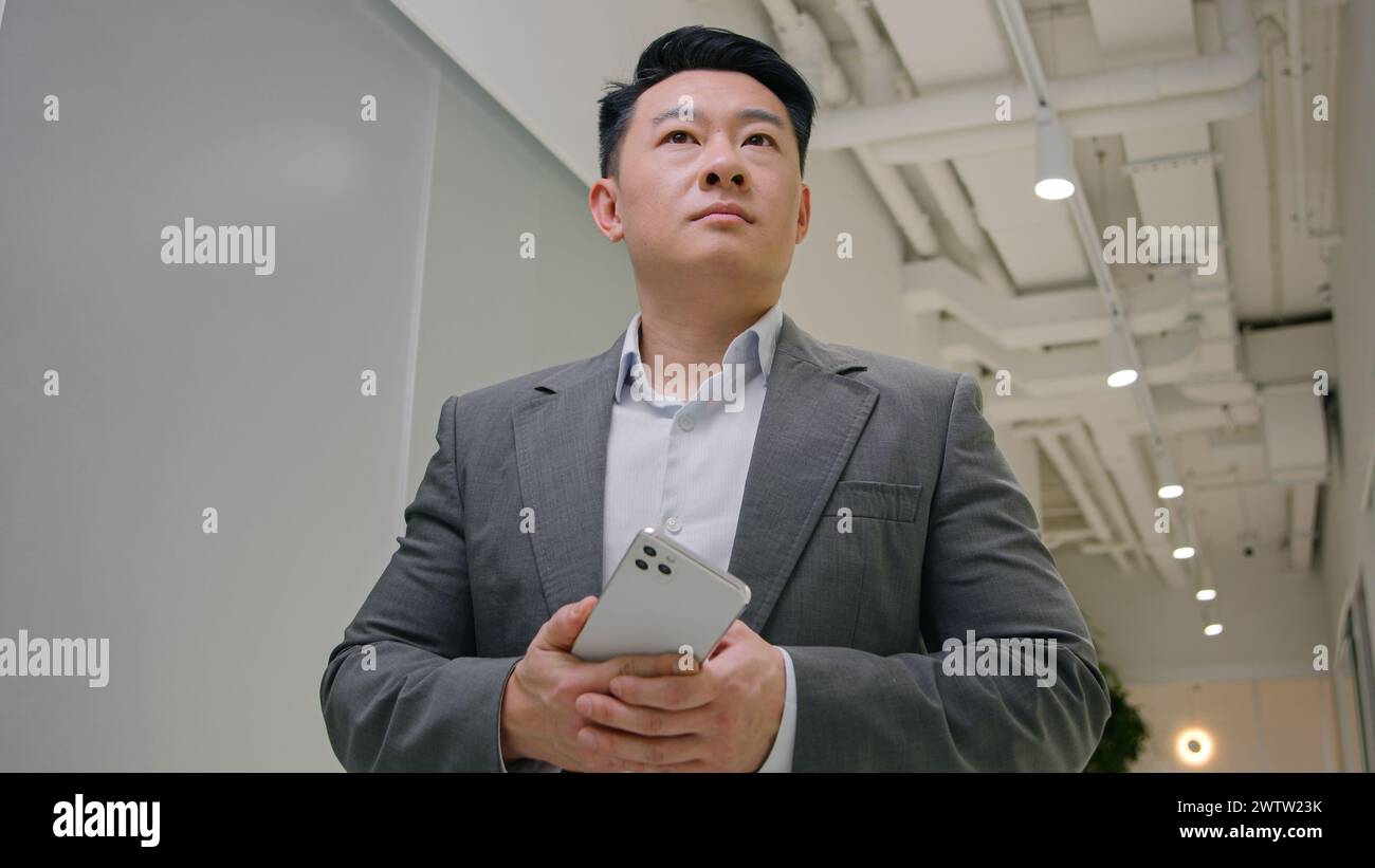 Thoughtful Asian adult 40s senior businessman browsing smartphone app ...