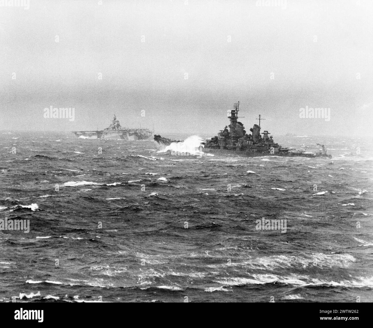 White foam swirls across the decks of the USS New Jersey, foreground ...