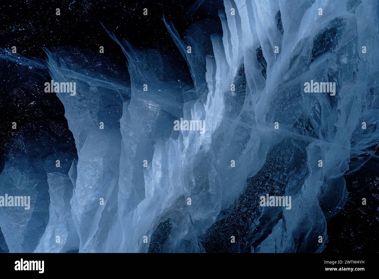 Transparent dark blue ice of frozen Baikal lake with white cracks ...