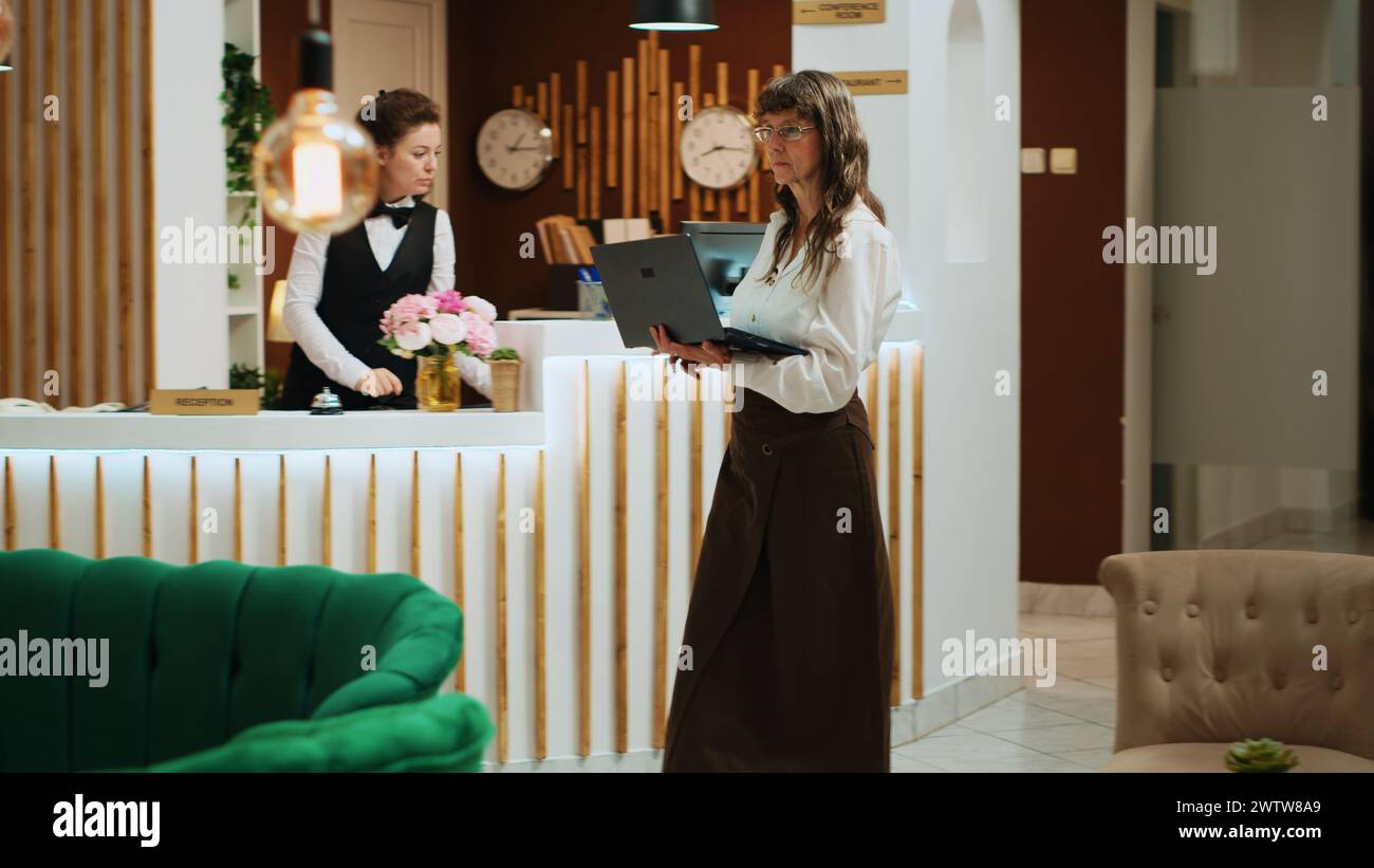 Senior woman using laptop in lobby lounge area, navigating online ... Senior woman using laptop in lobby lounge area, navigating online ...