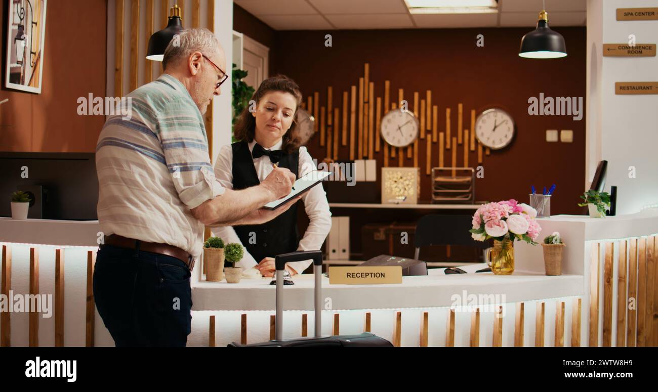 Old person signing check in forms at front desk, finishing with ...