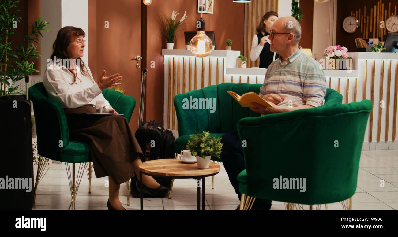 Elderly couple talk about vacation plans in hotel lounge area, waiting ...