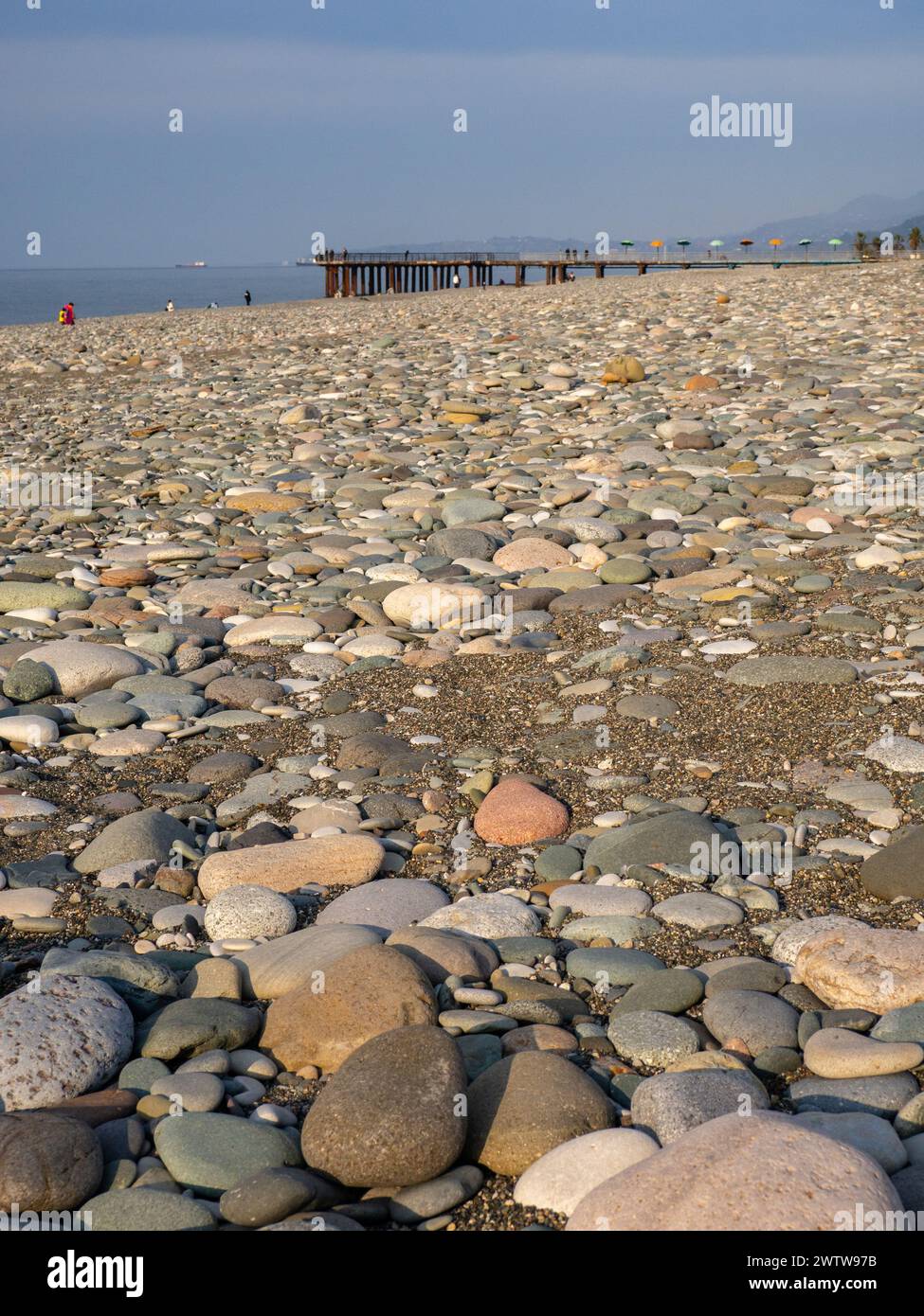 Gray sand and stones on the beach. Long pier on the seashore. Beach in ...