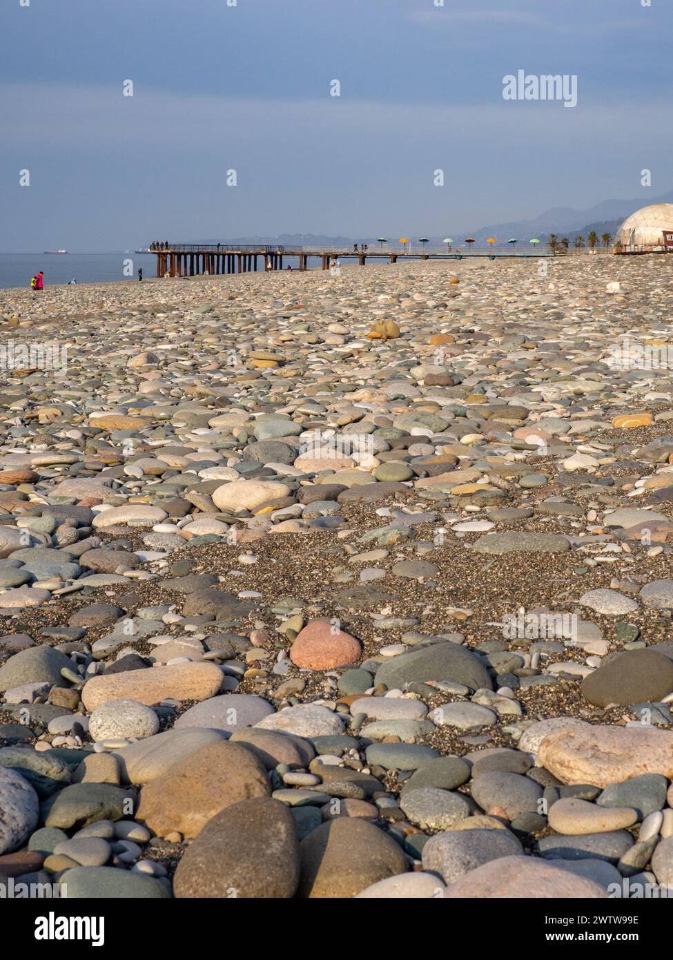 Gray sand and stones on the beach. Long pier on the seashore. Beach in ...