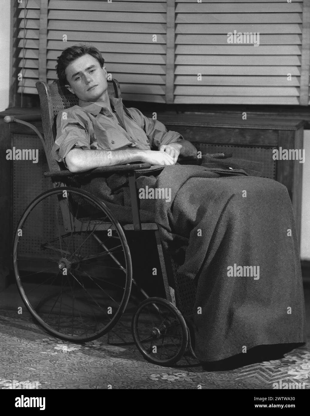 Young Man Sitting In A Wheelchair With A Blanket Wrapped Around Him Arms Folded Looking