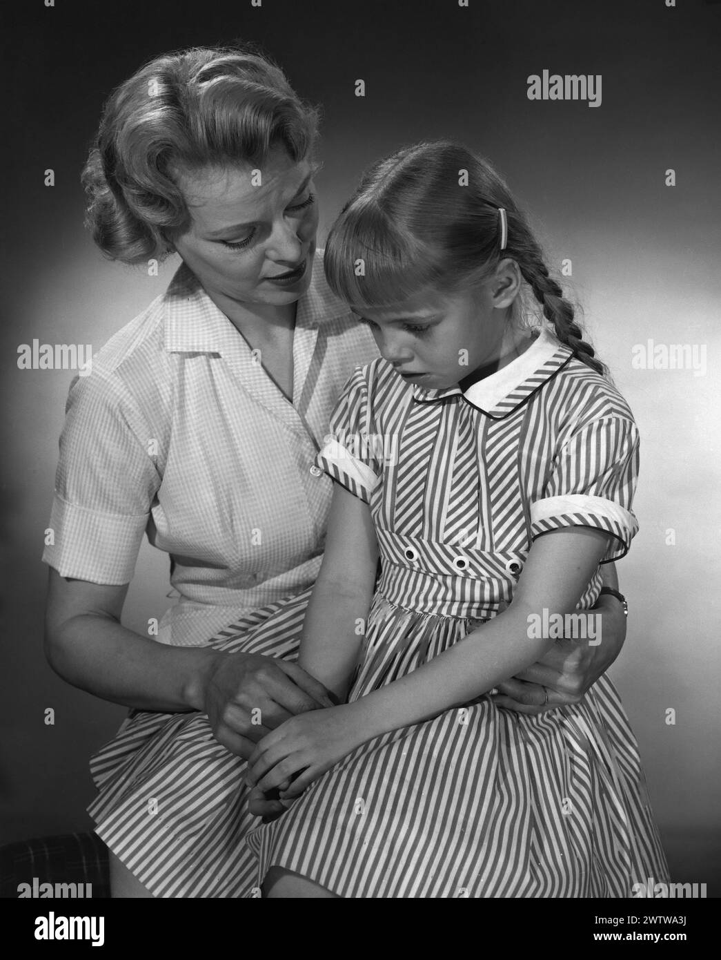 Middle-aged mother with older child, girl sitting on her lap, glancing ...