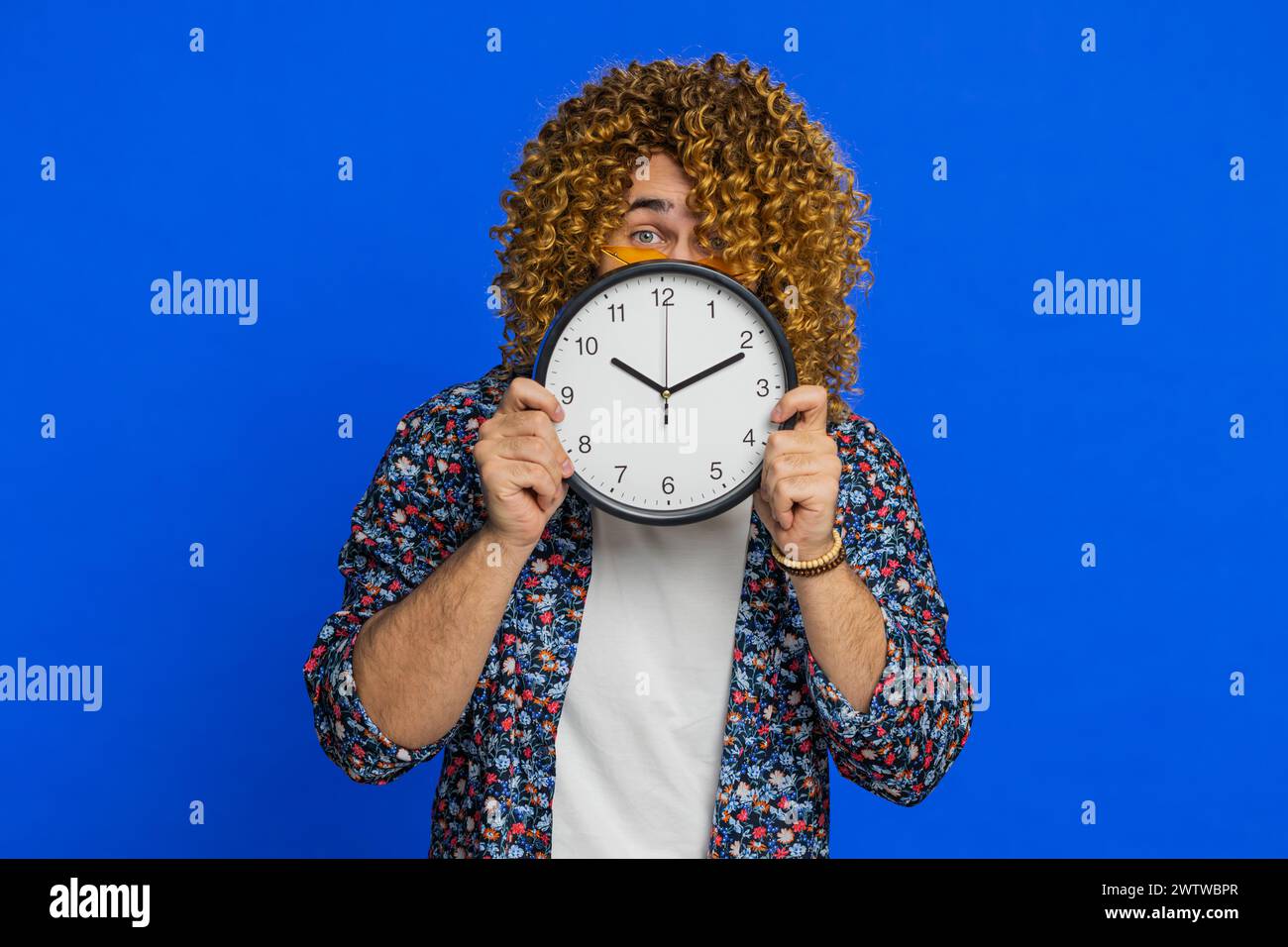 Serious strict man with curly hairstyle wig holding office clock hiding ...