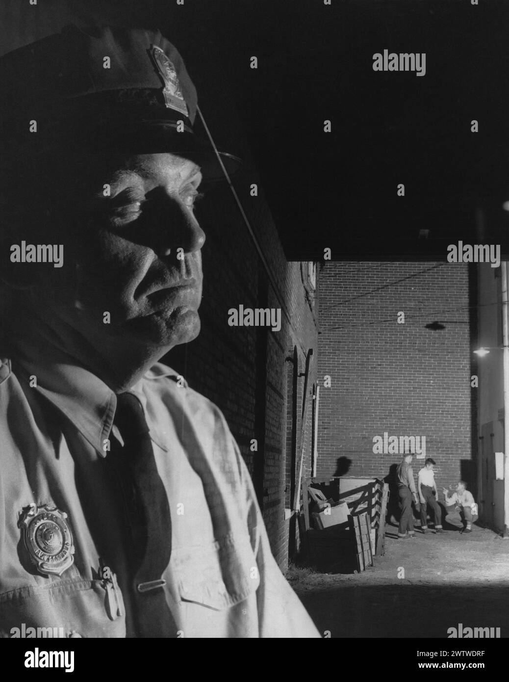 Police man hiding in the shadows of a back alley. Watching a group of ...