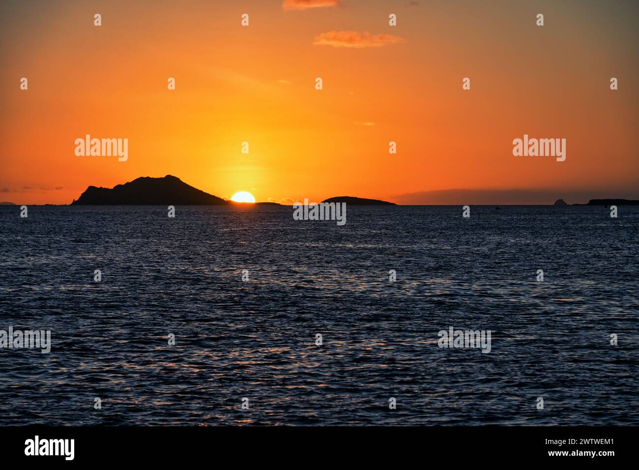 The sun sets perfectly between two land features, creating a stunning ...