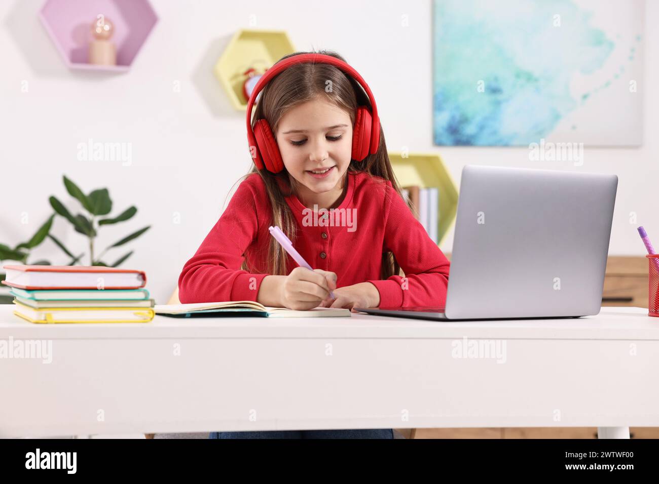E-learning. Cute girl taking notes during online lesson at table ...
