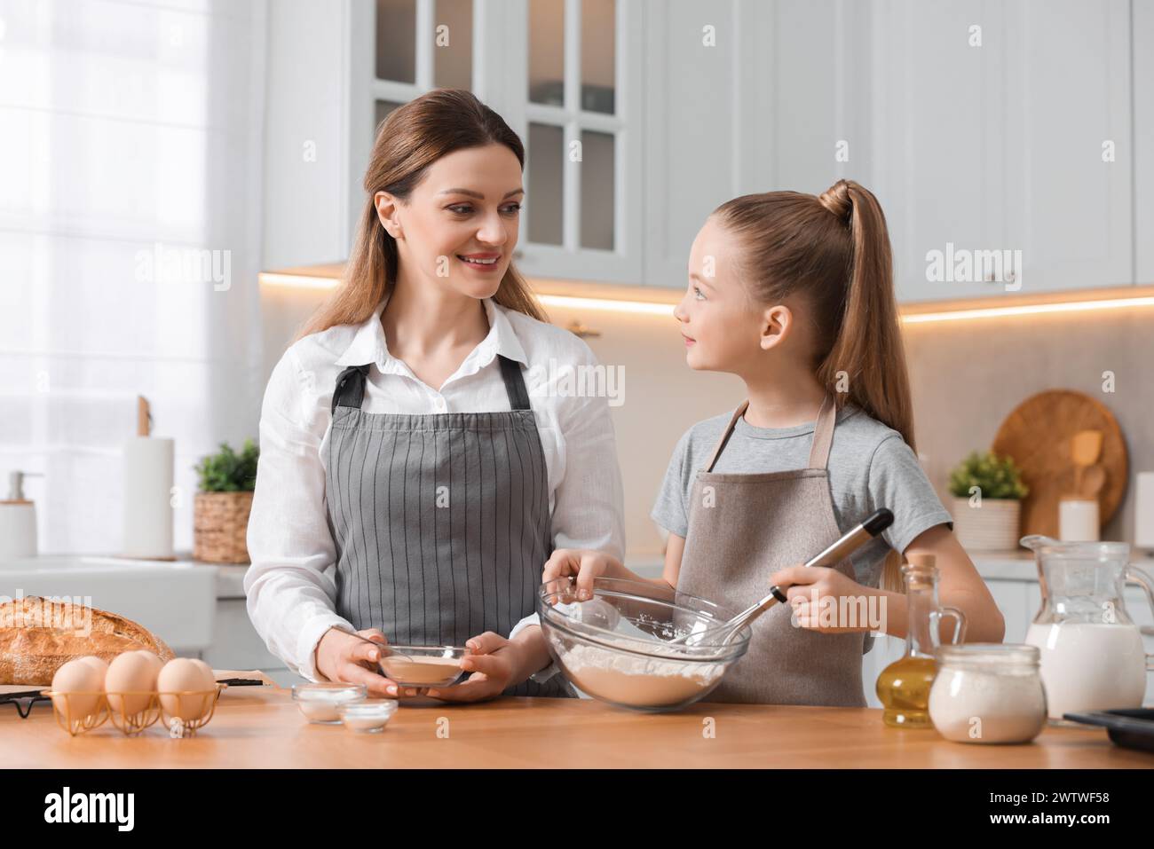 Making bread. Mother and her daughter putting flour and dry yeast into ...