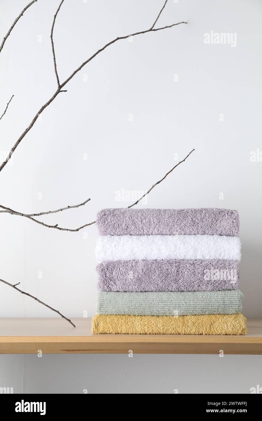 Stacked terry towels and tree branch on wooden shelf near white wall ...