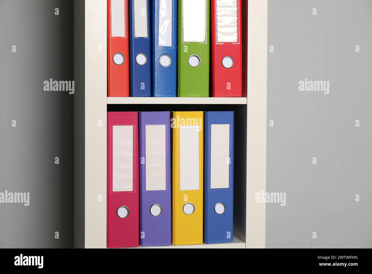 Colorful binder office folders on shelving unit near light grey wall ...