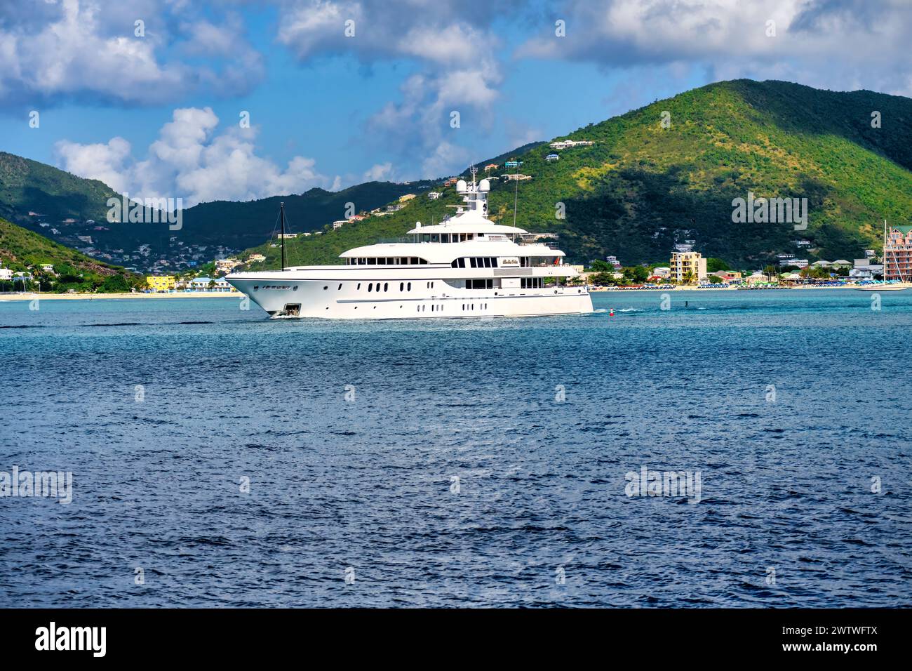 A luxury yacht cruises the clear blue waters of the Caribbean with lush ...
