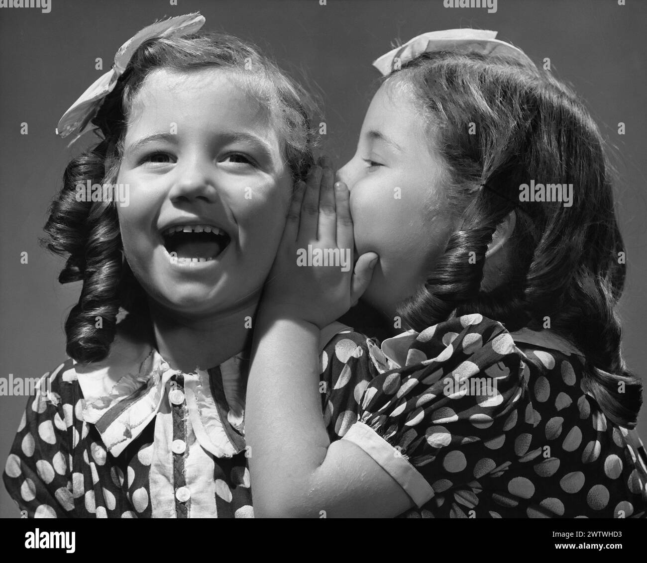 Two young twin girls dressed alike with polk-a-dot dresses and a bow in ...