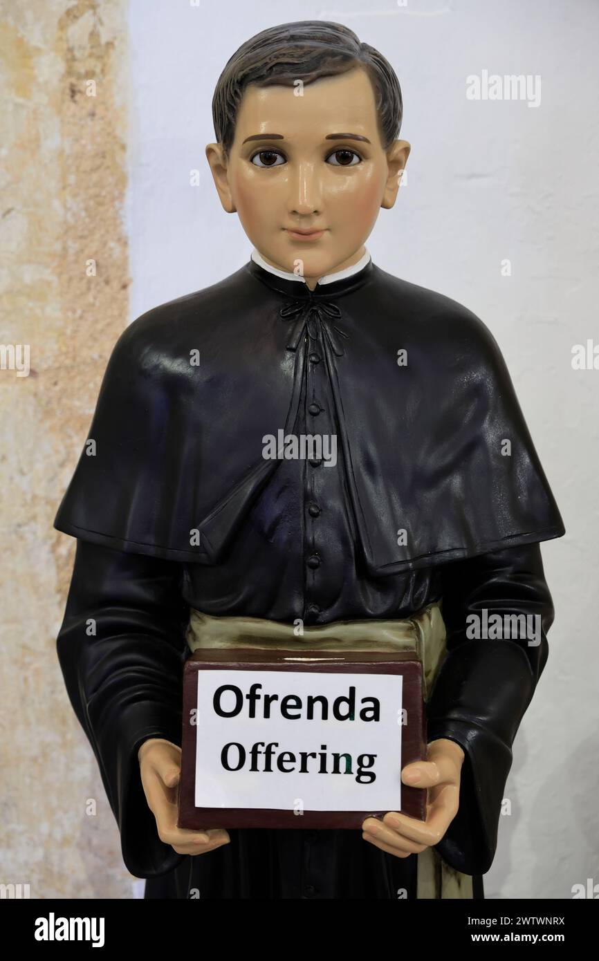 The statue of an altar server holding a offering box inside of ...