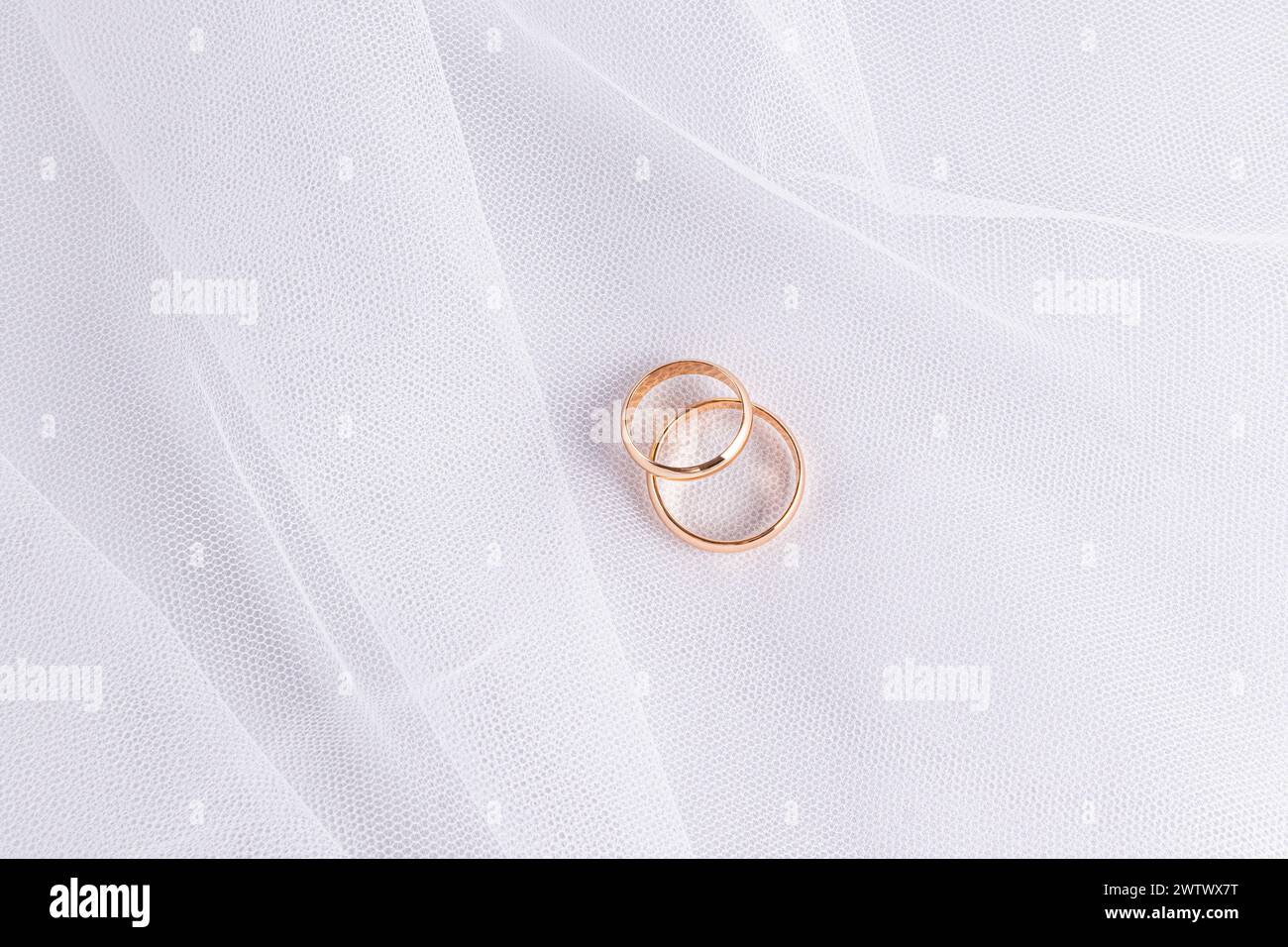 Two gold wedding rings lie on the folds of a white classic bridal veil ...