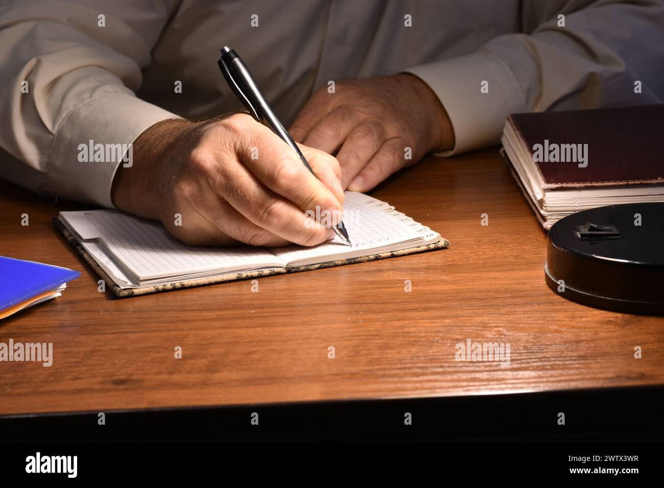 The picture shows a man who is sitting at a table and writing in a ...
