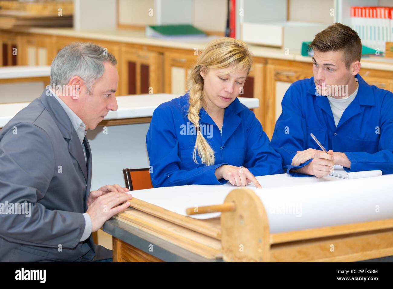 students wearing blue jackets sat at desk talking to teacher Stock ...