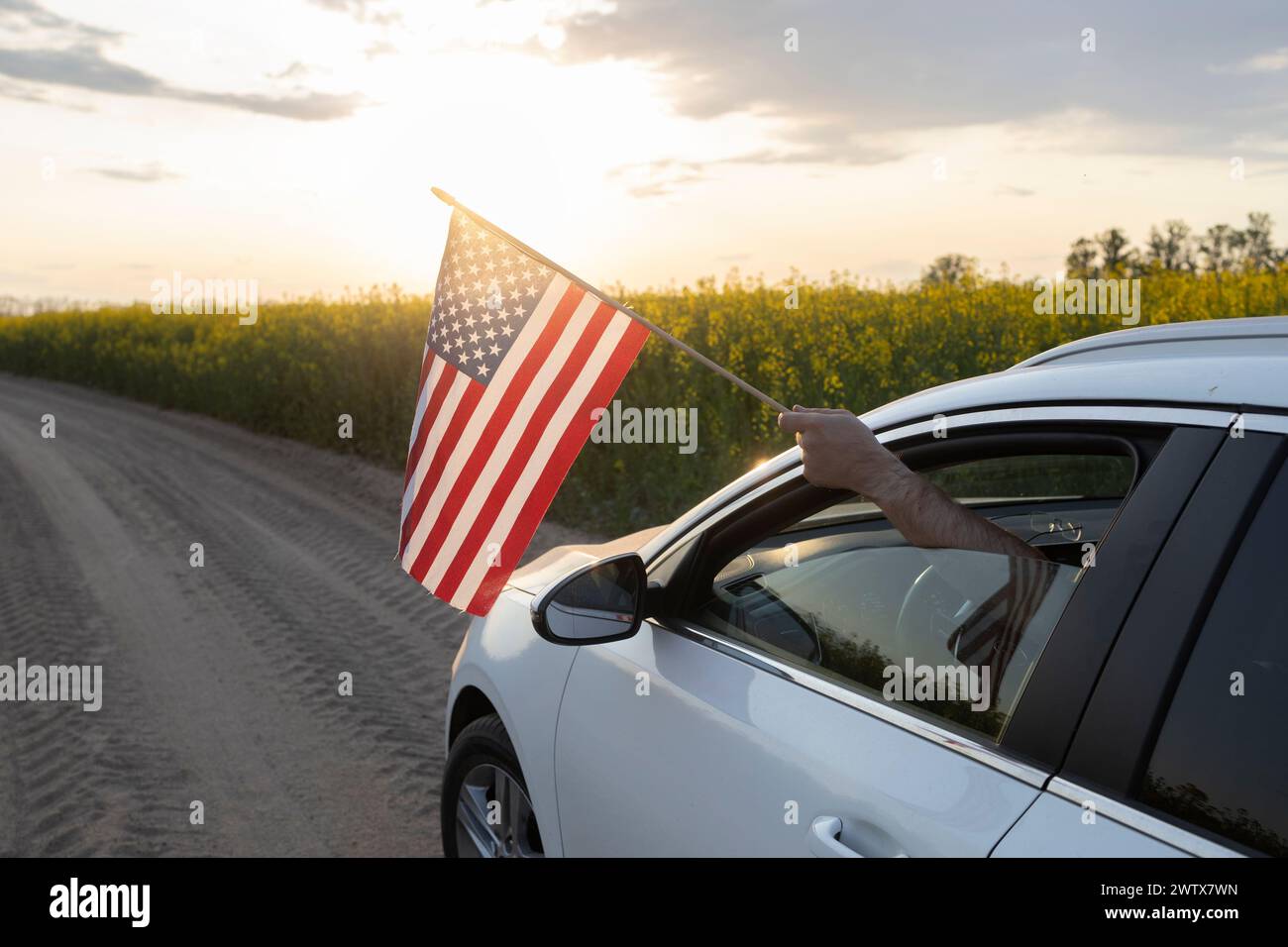 car with an American flag hanging from the window drives along country ...
