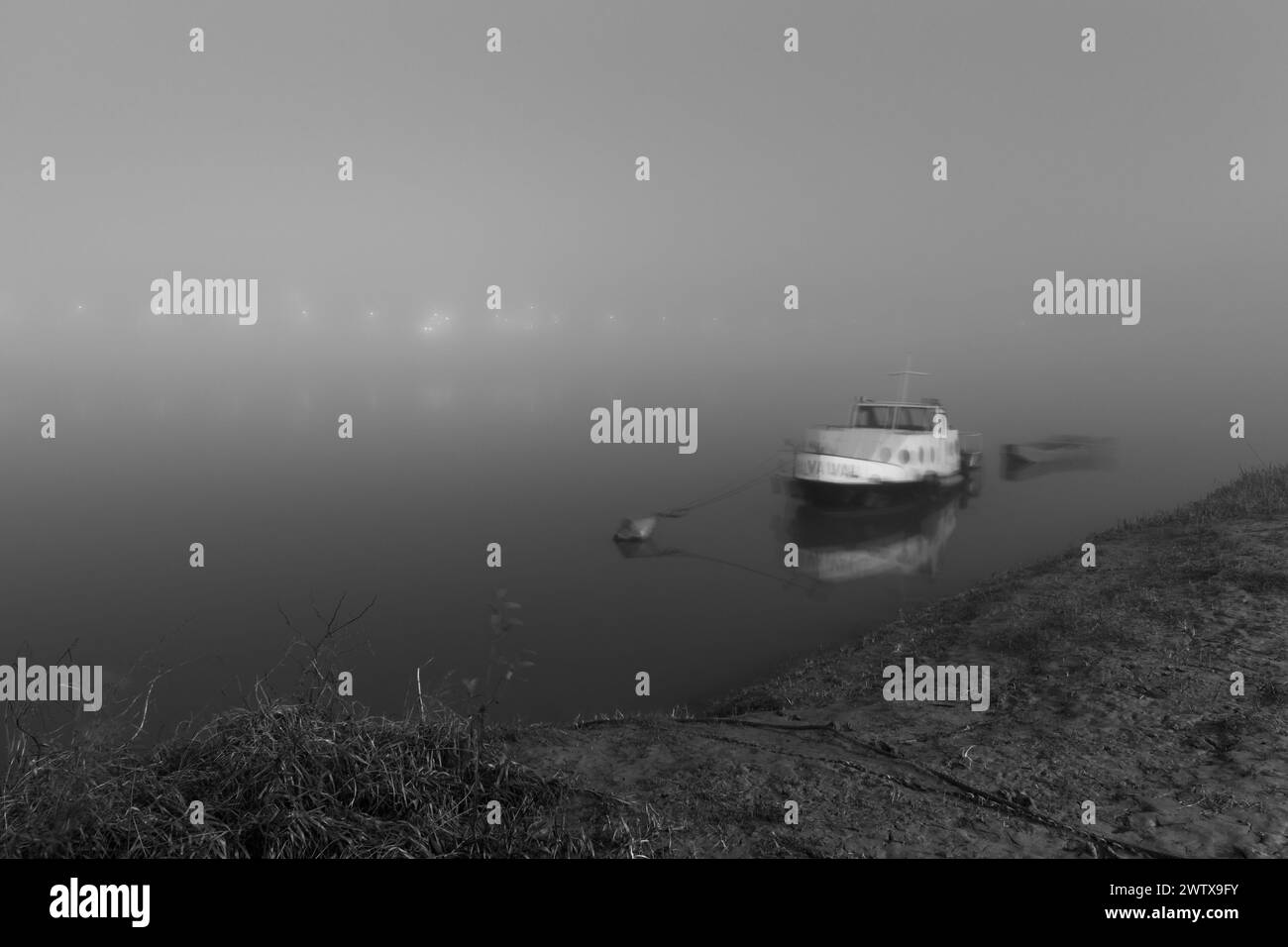 Anchored boats near riverbank in fog at night illuminated with lights ...