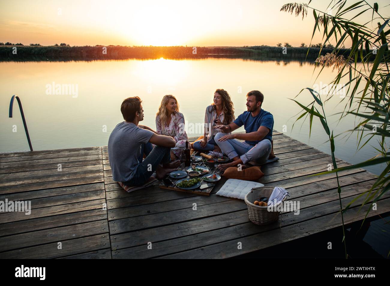 Group of friends having fun on picnic near a lake, sitting on pier ...