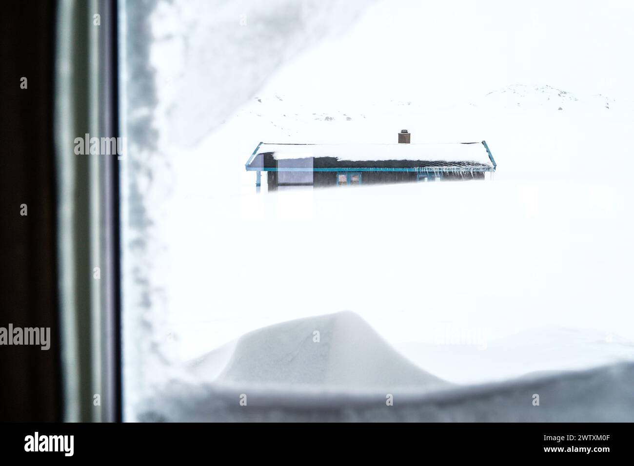 looking out of a mountain cabin window to another hut covered by winter ...