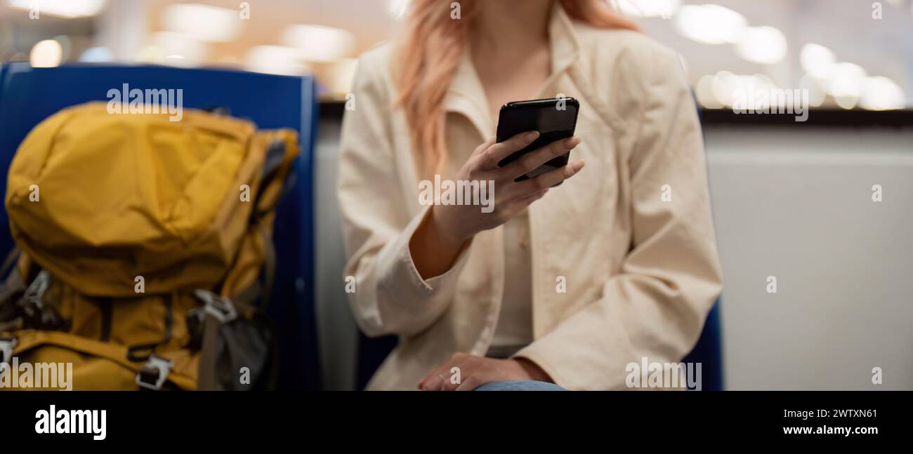 Tourist woman using mobile smartphone with suitcase traveling between waits for flight in ...