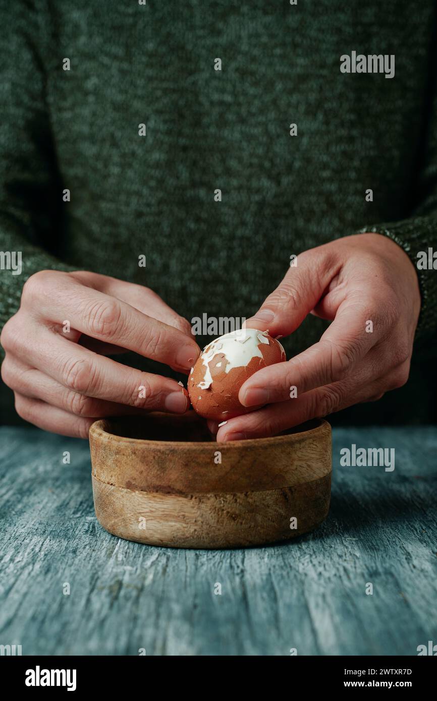 closeup of a man peeling a brown boiled egg at a rustic gray wooden ...
