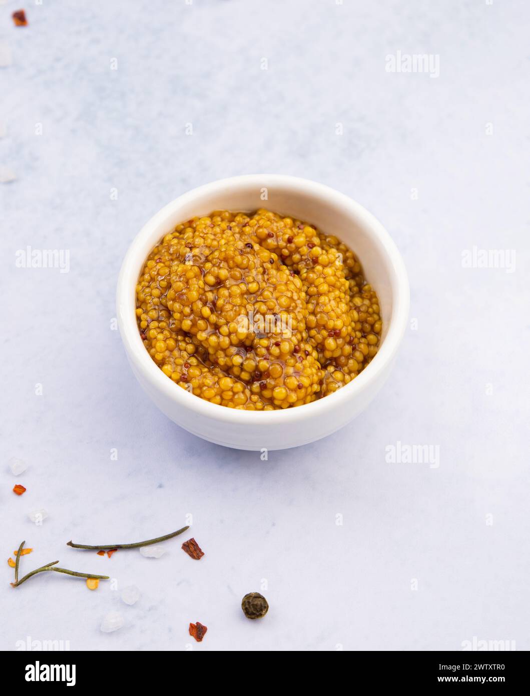 grainy mustard in a white ceramic bowl on a blue table surrounded by ...