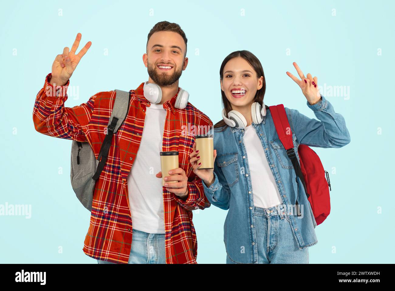 couple students with backpacks and coffee gesturing victory signs ...