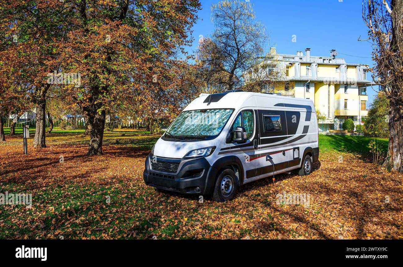 Camper van or motor home is parked in city camping under the trees in ...