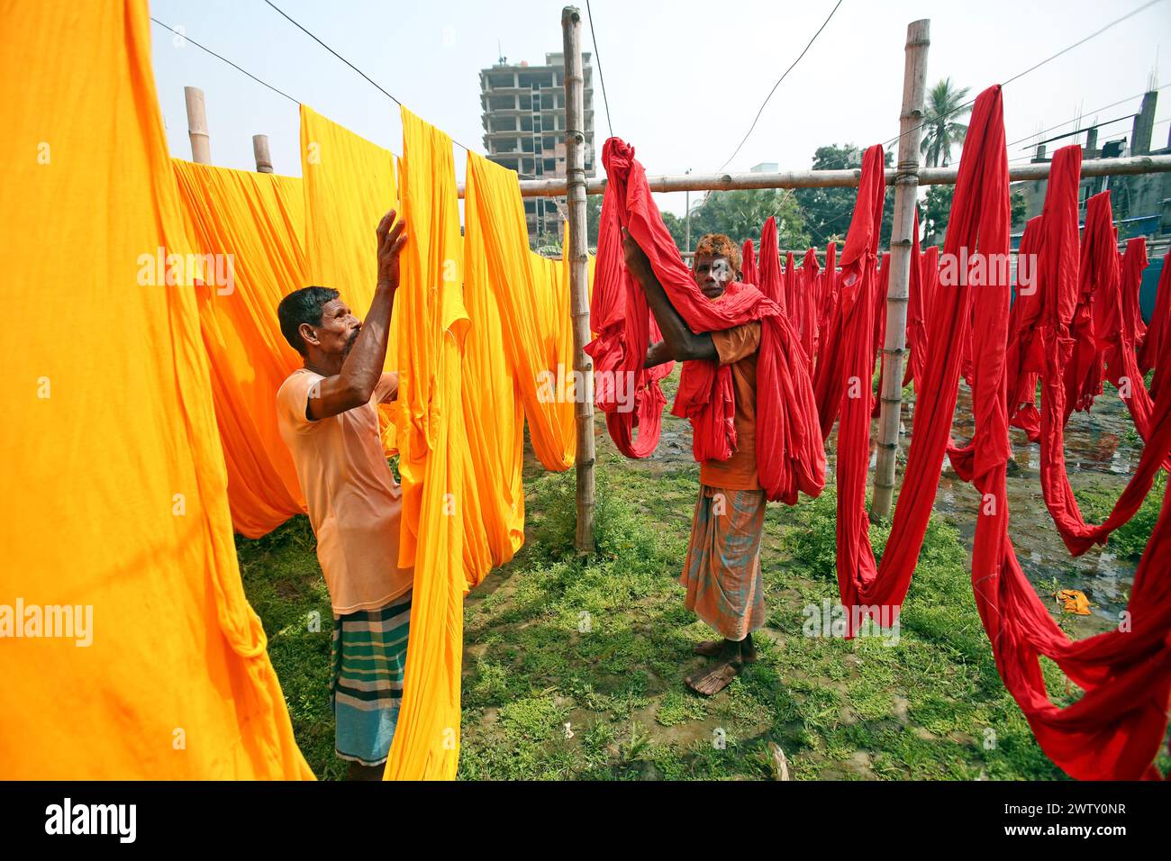 Bangladeshi workers collect fabric after drying them under the sun at a ...