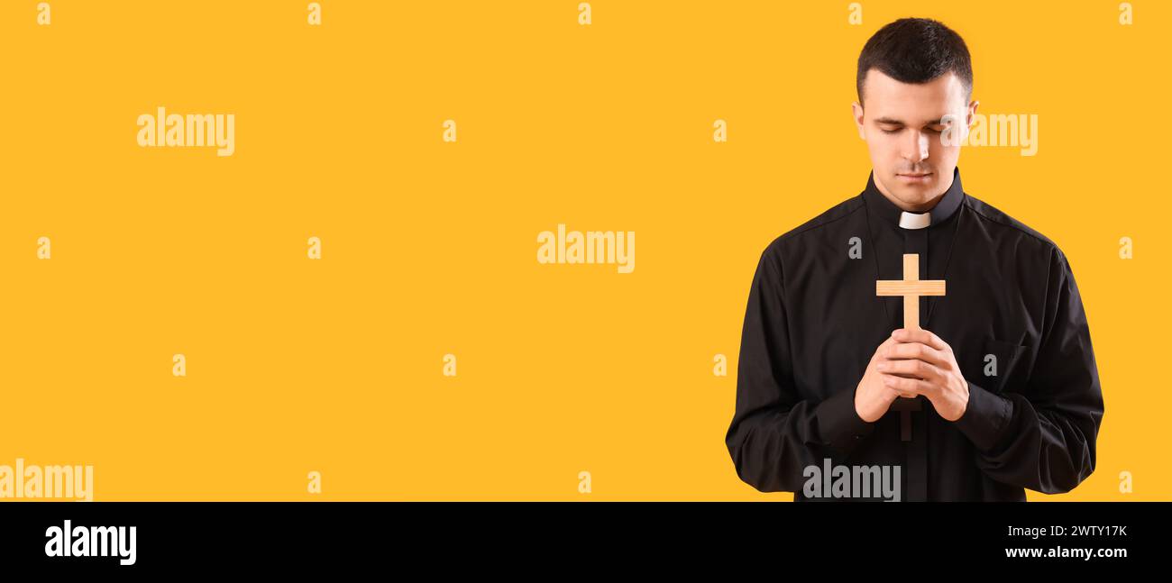 Young priest with cross praying on yellow background with space for ...