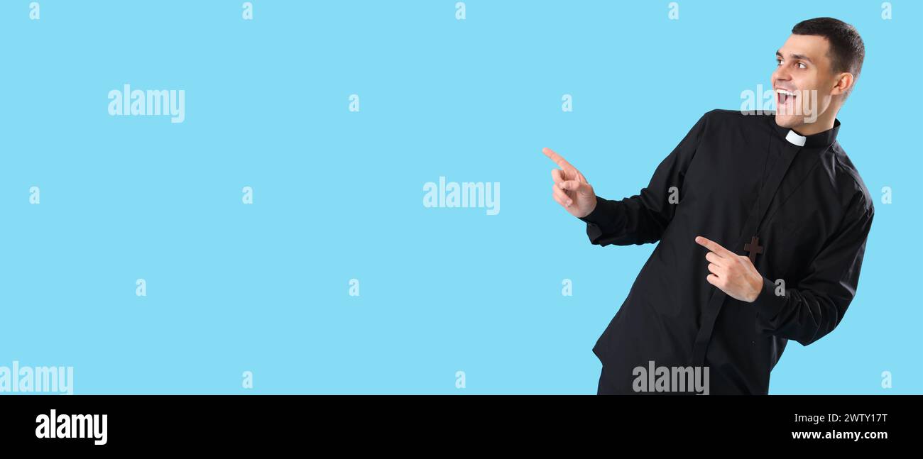 Happy young priest pointing at something on light blue background with ...