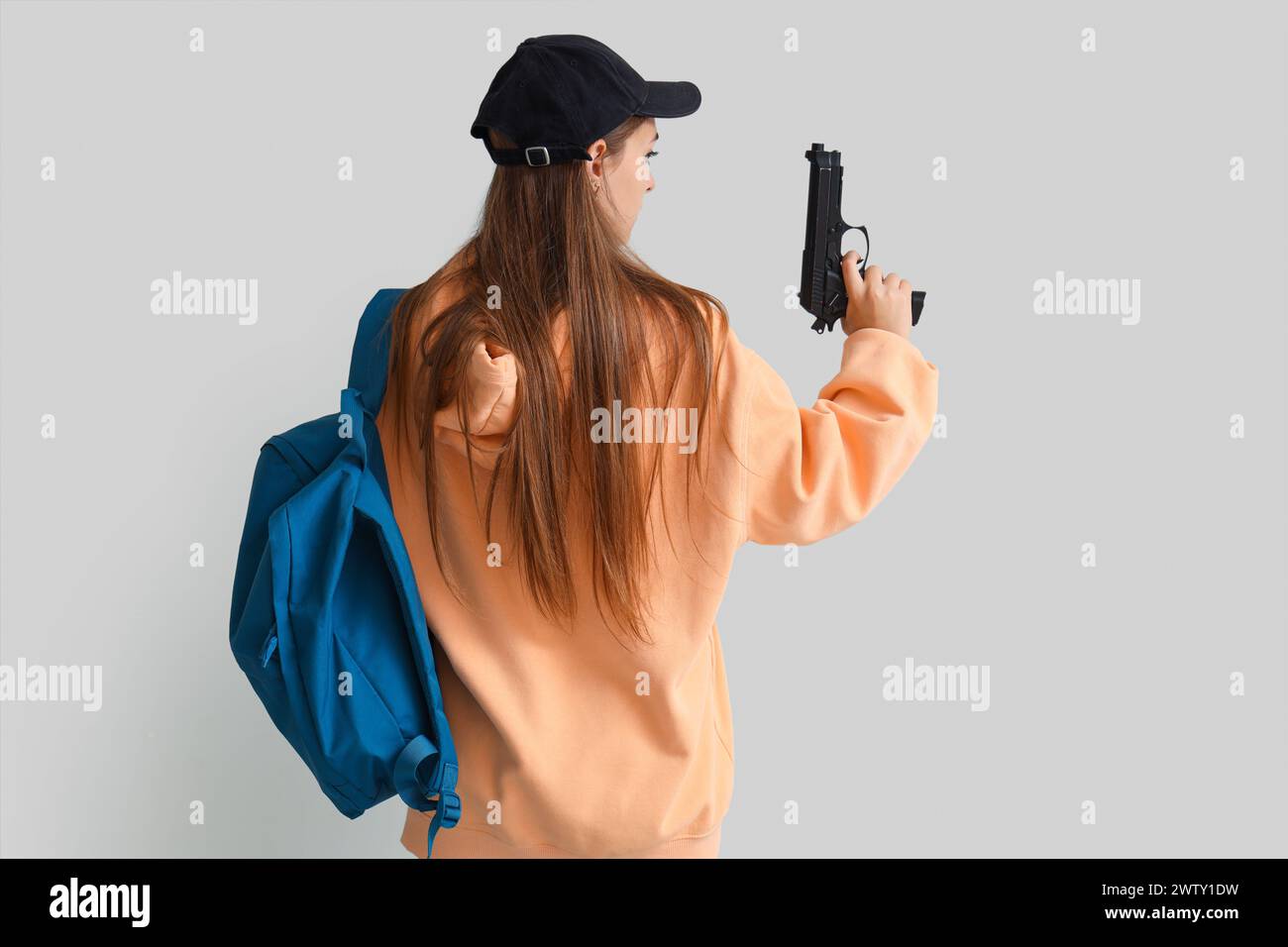 Female student with gun near light wall, back view. School shooting ...
