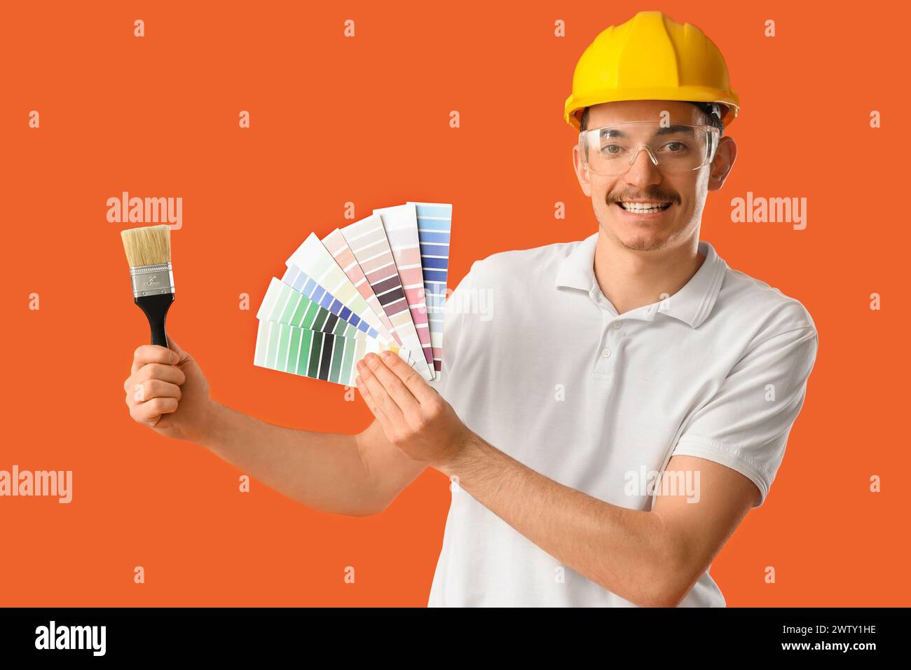 Male worker with paint color palettes and brush on orange background ...