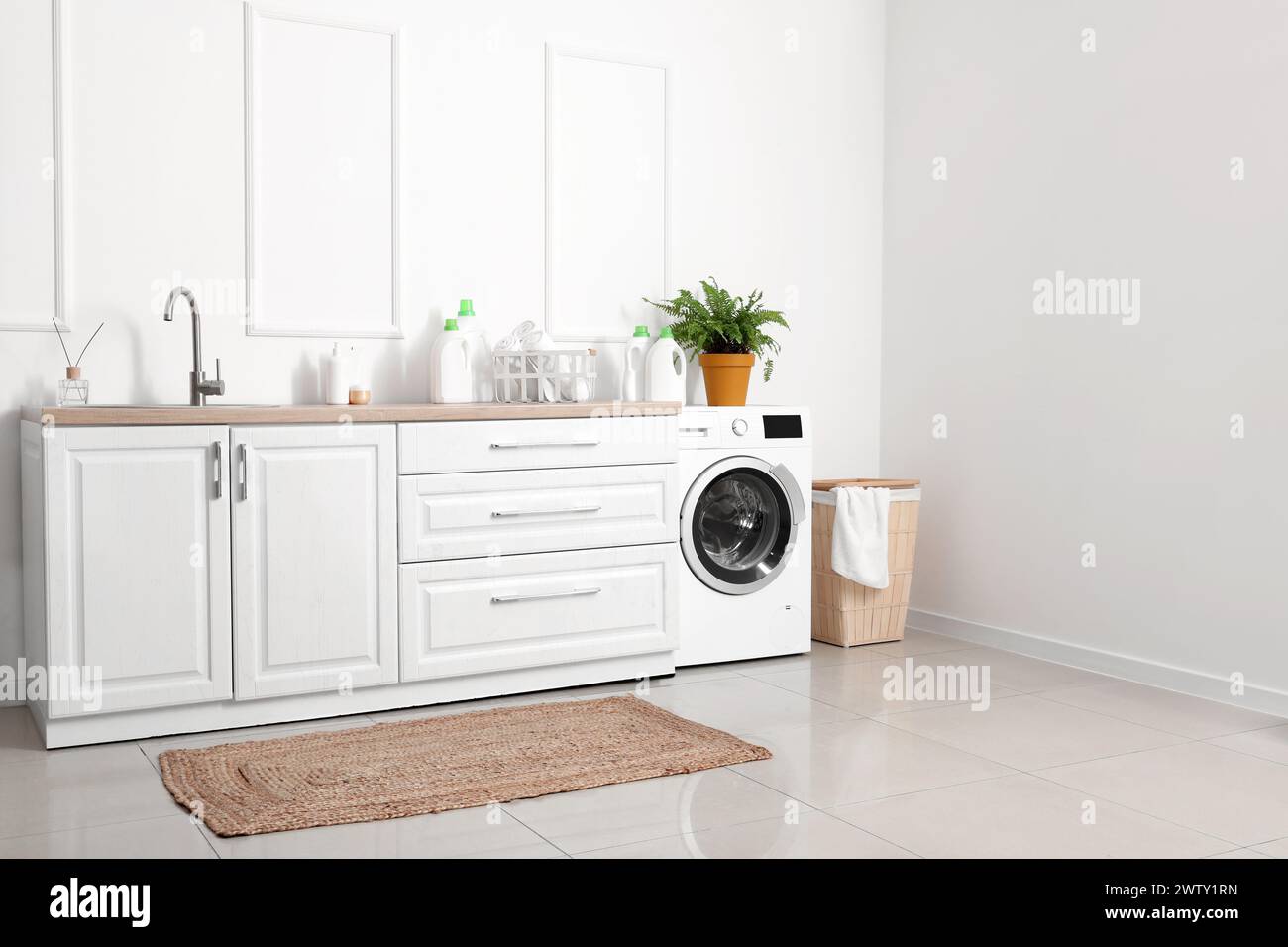 Interior of light room with sink, washing machine and laundry basket ...
