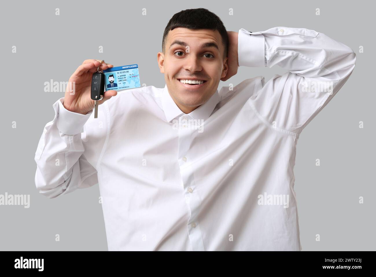 Young surprised man holding driver license and car key on grey ...