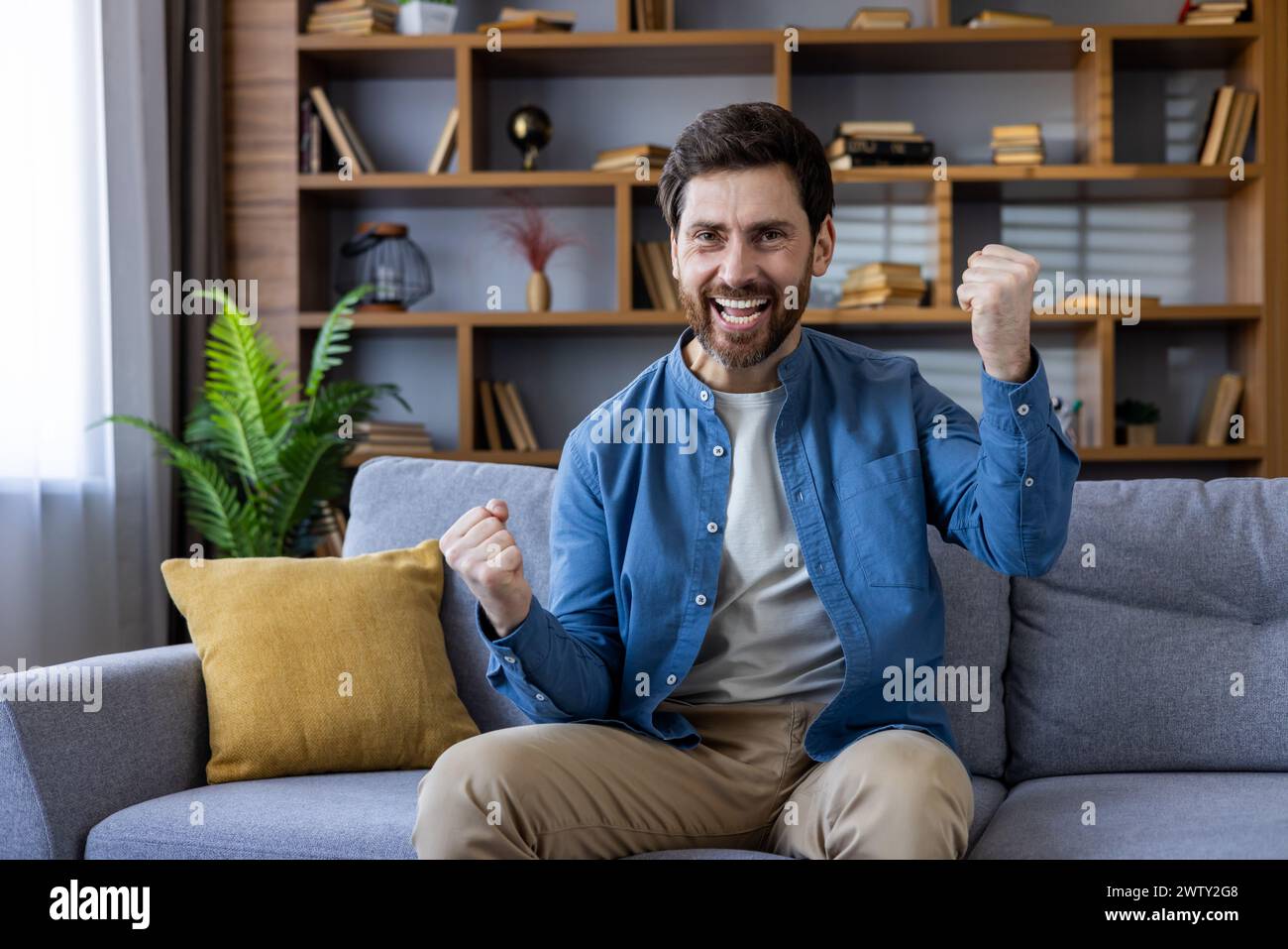 A joyful moment captured of a man seated on a gray sofa in a cozy ...
