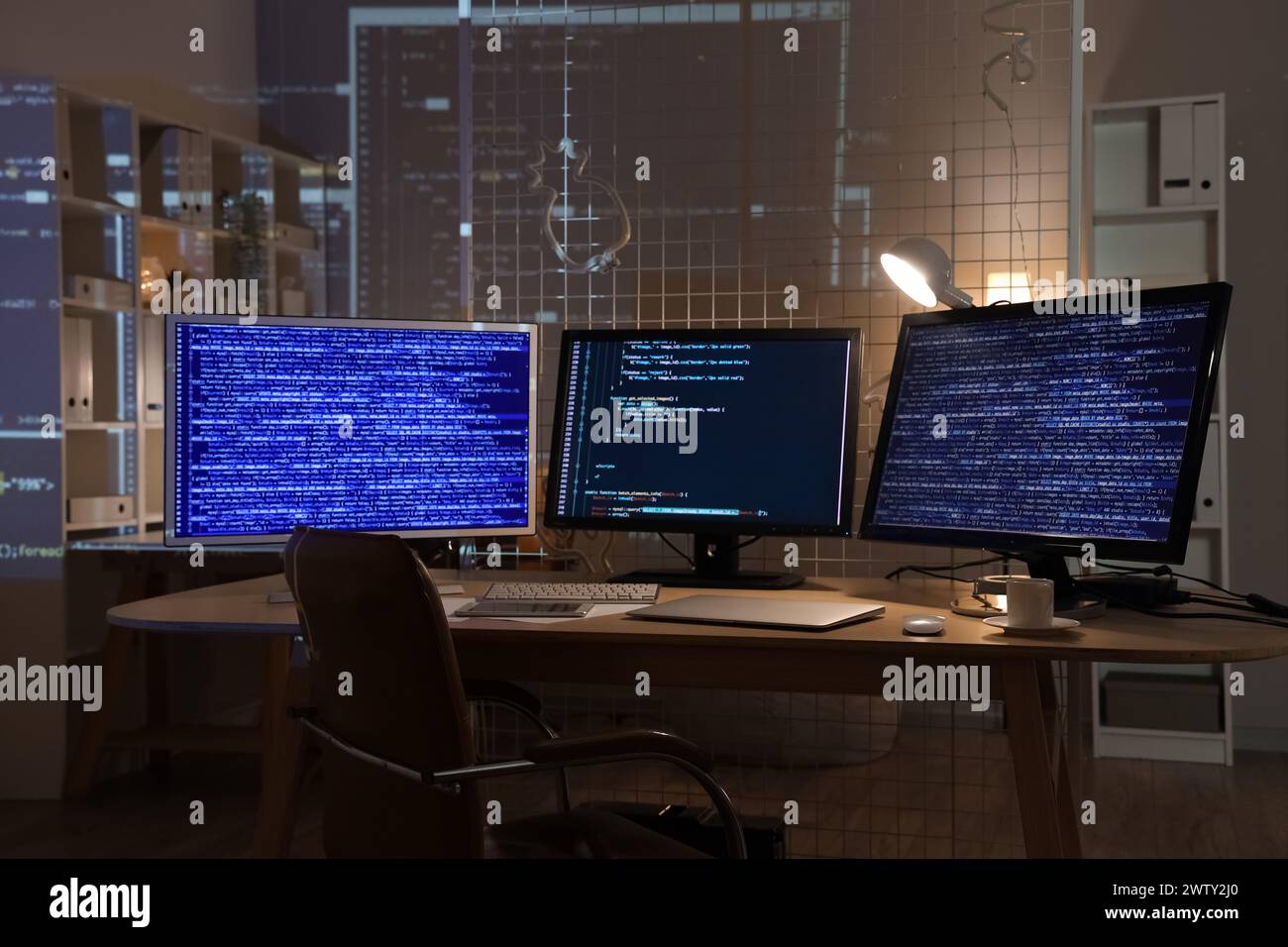 Computer monitors with programming code on table in office at night ...