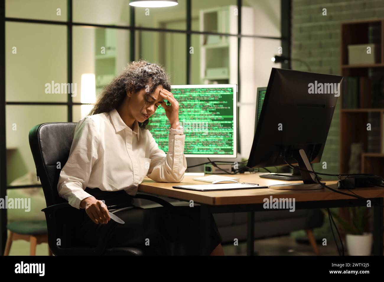 Tired female African-American programmer sitting in office at night ...