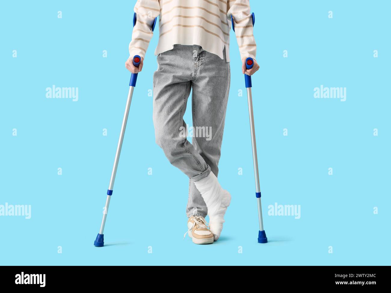Injured young woman after accident with crutches on blue background ...
