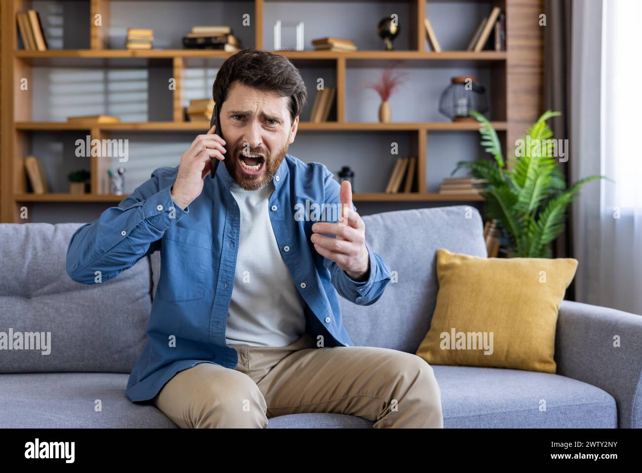 An agitated adult male sits on a couch, gesturing in frustration during ...
