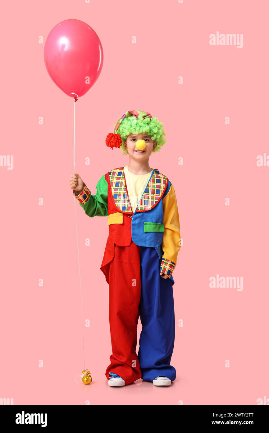Funny little boy in clown costume with balloon on pink background ...